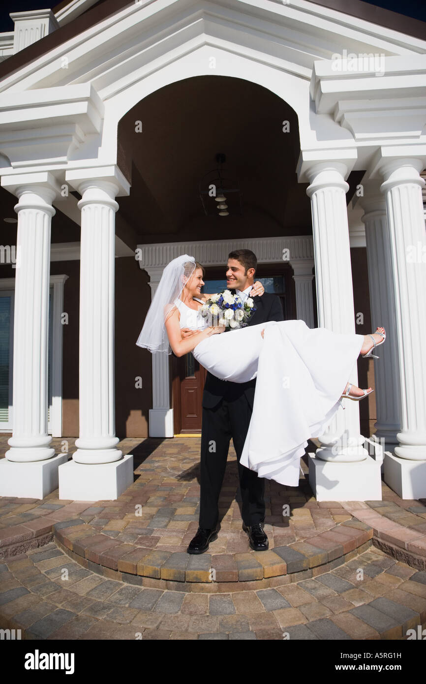 Young man carrying his bride in his arms in front of a building Stock ...