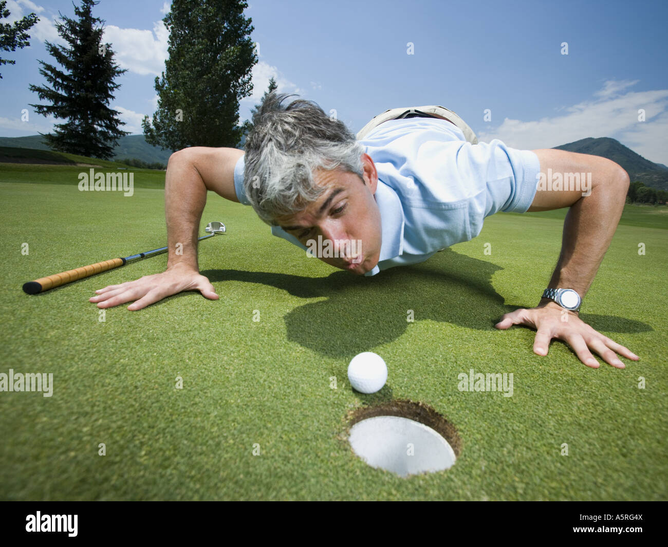Close up of a man blowing a golf ball towards a hole Stock Photo - Alamy