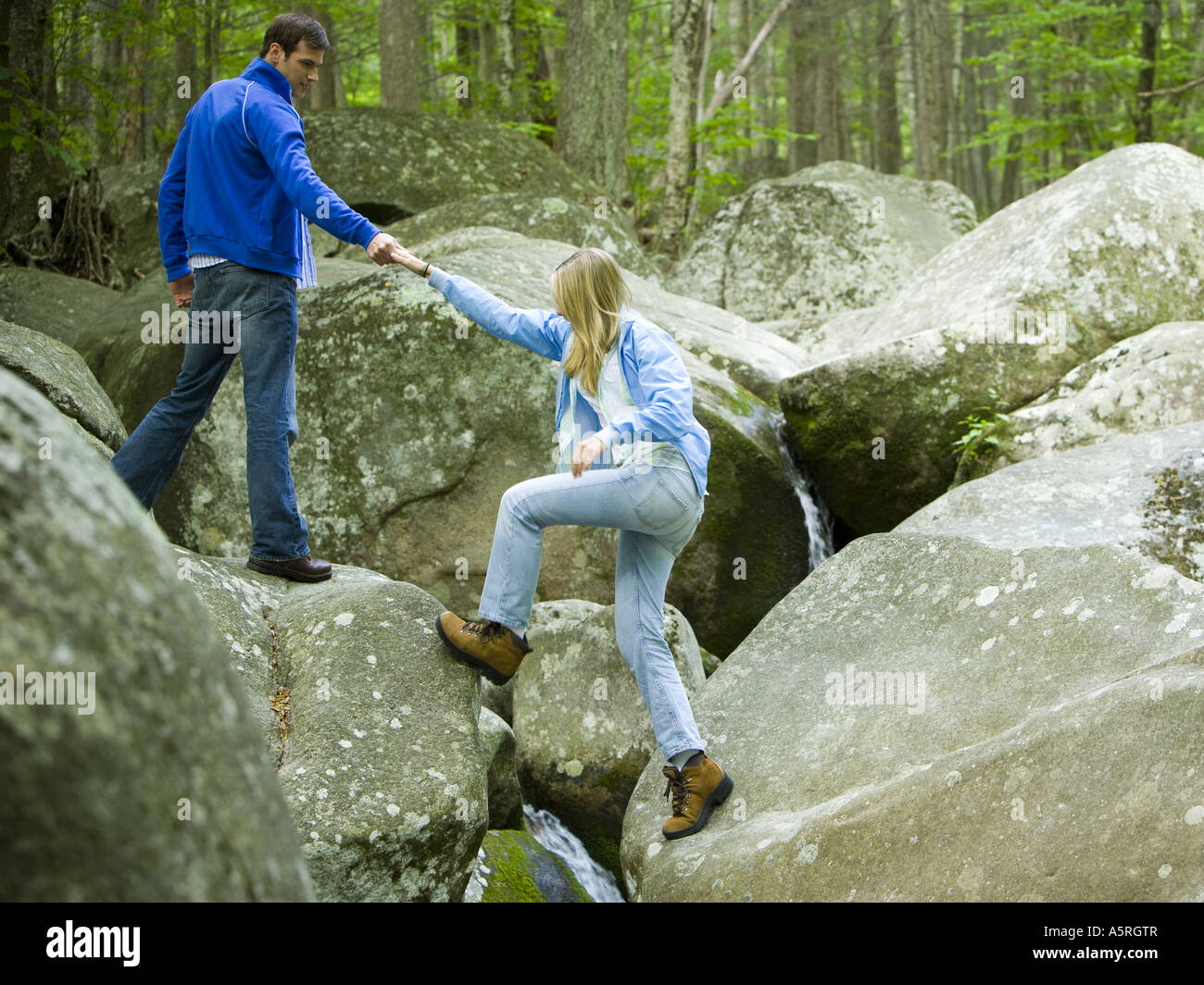 Young man helping a young woman climb a rock Stock Photo - Alamy