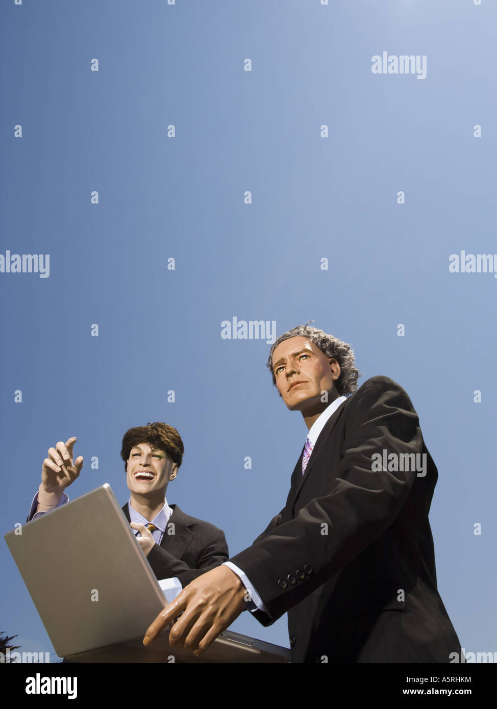 Low angle view of two mannequins portraying businessmen using a laptop ...
