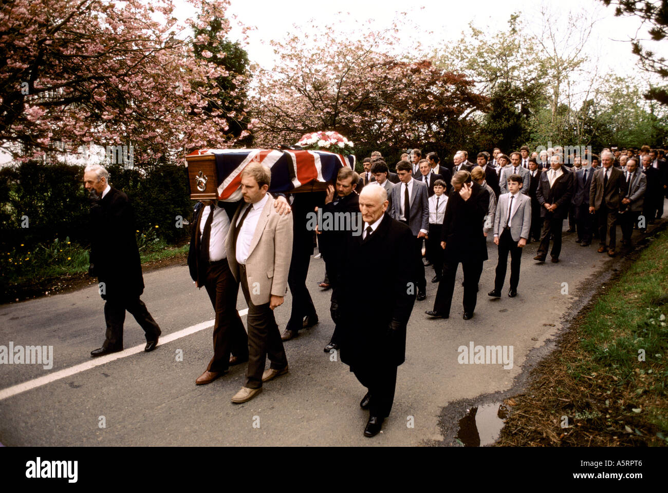 CORTEGE FOLLOWING MEN BEARING THE COFFIN WALKING ALONG COUNTRYSIDE ROAD ...