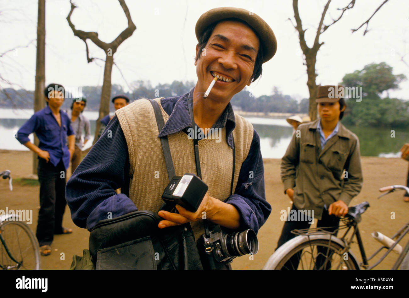 VIETNAM, A SMILING PHOTOGRAPHER CARRYING HIS CAMERA FLASH SMOKES A ...