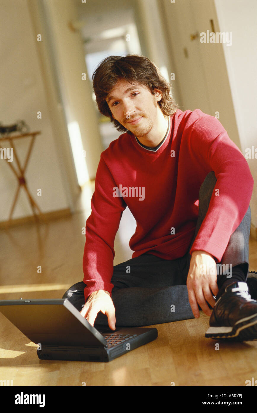 Young man sitting on floor, using laptop Stock Photo - Alamy