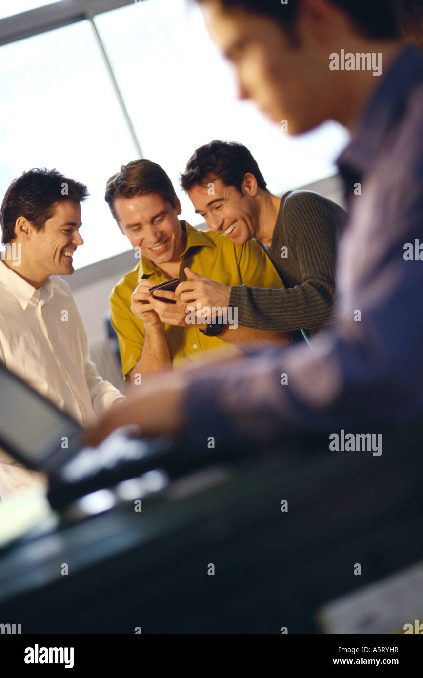 Three young men using electronic organizer, laptop user in foreground ...