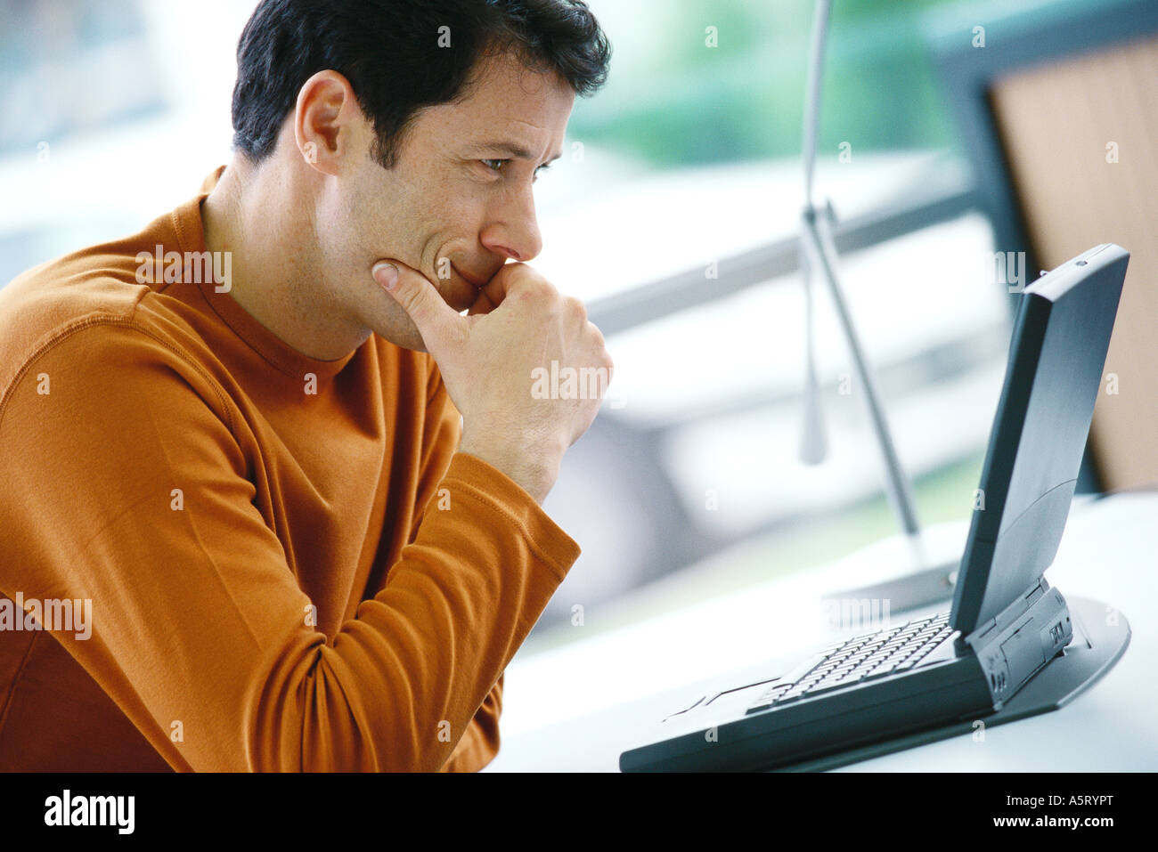 Man using laptop, hand over mouth, smiling Stock Photo - Alamy