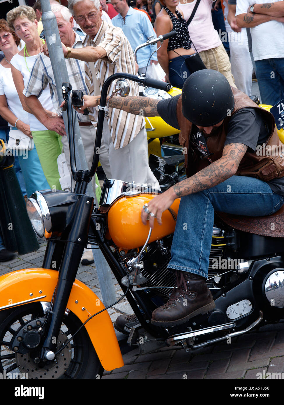 a heavily tattooed biker putting his orange classic chopper motorcycle ...
