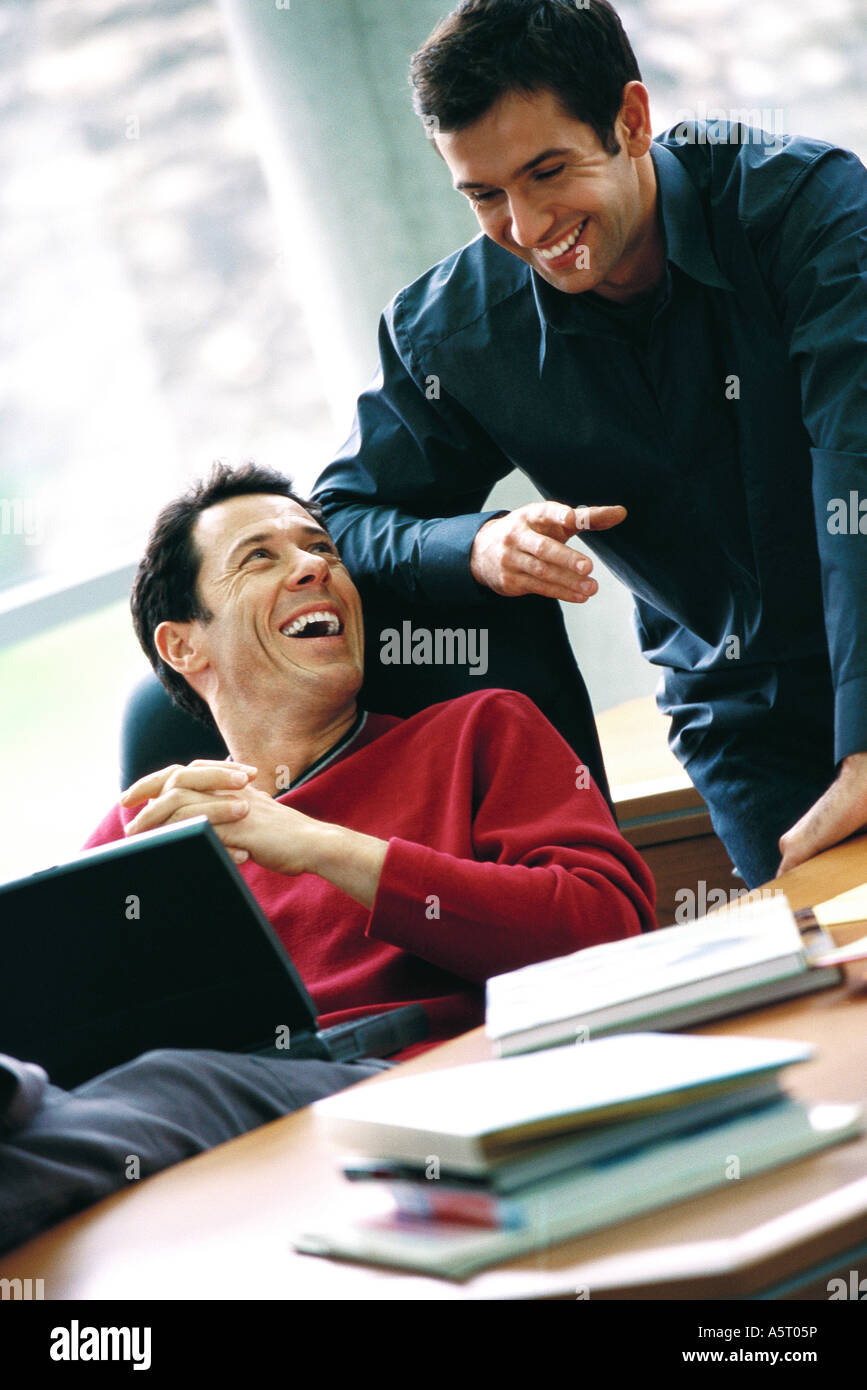Man using laptop, looking at second man looking over shoulder, laughing ...