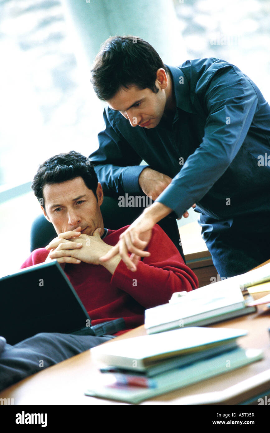 Man using laptop, second man leaning over shoulder, pointing at screen ...
