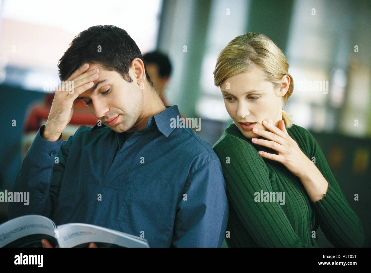 Man looking at brochure, holding head, woman looking over his shoulder ...