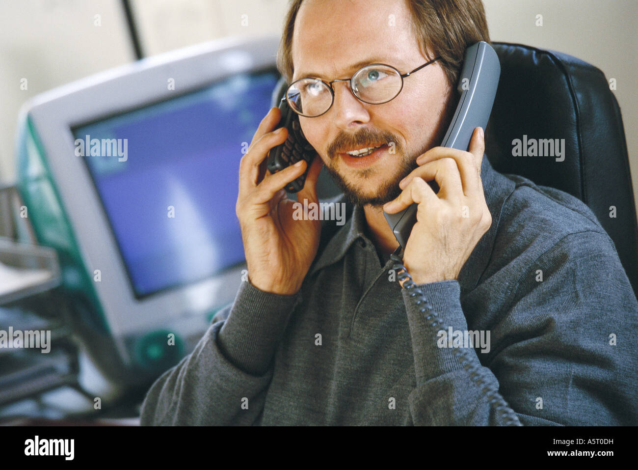 Man in office using cell phone and landline phone at same time Stock ...