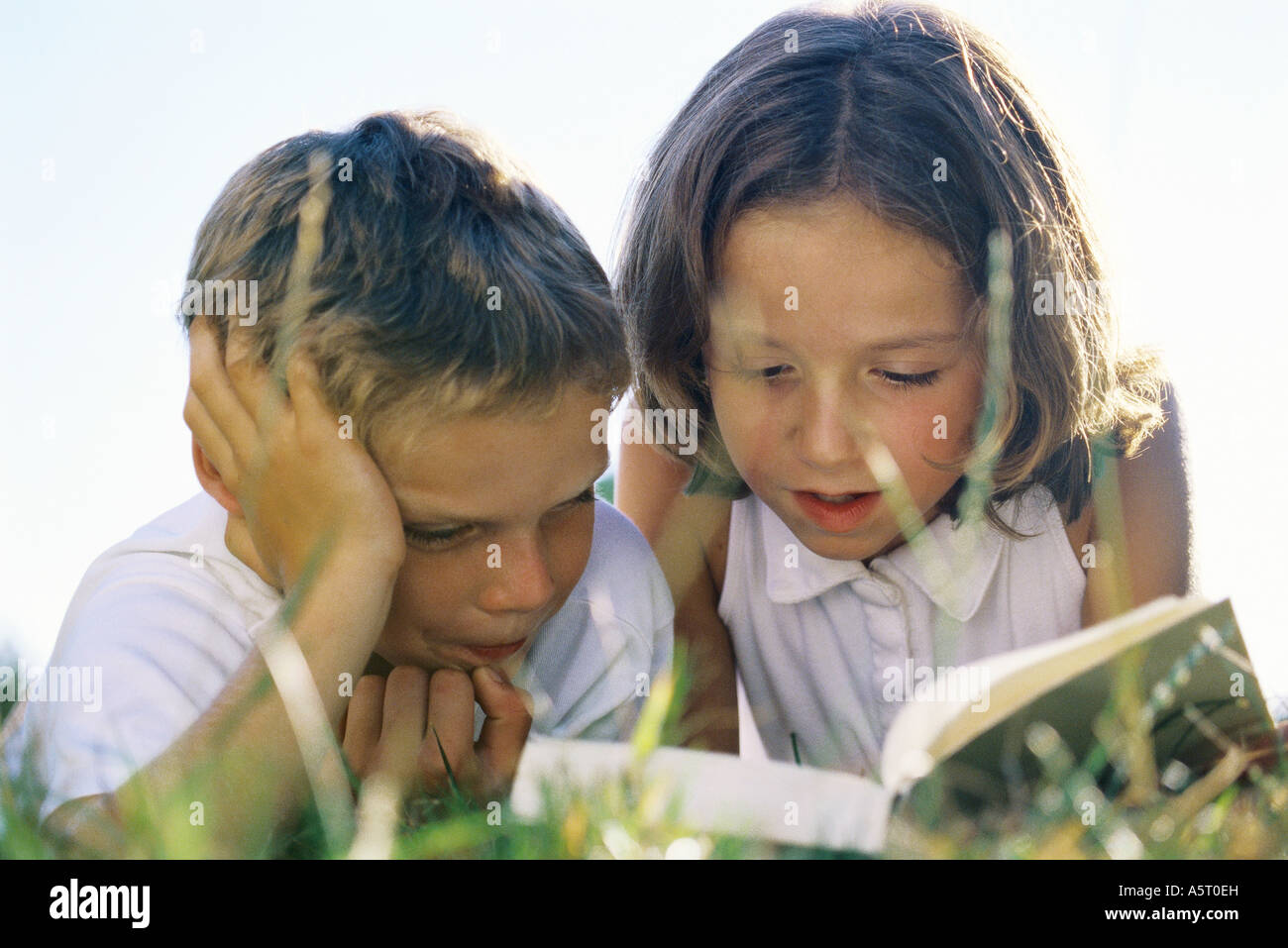 Two children reading book together, in grass Stock Photo - Alamy