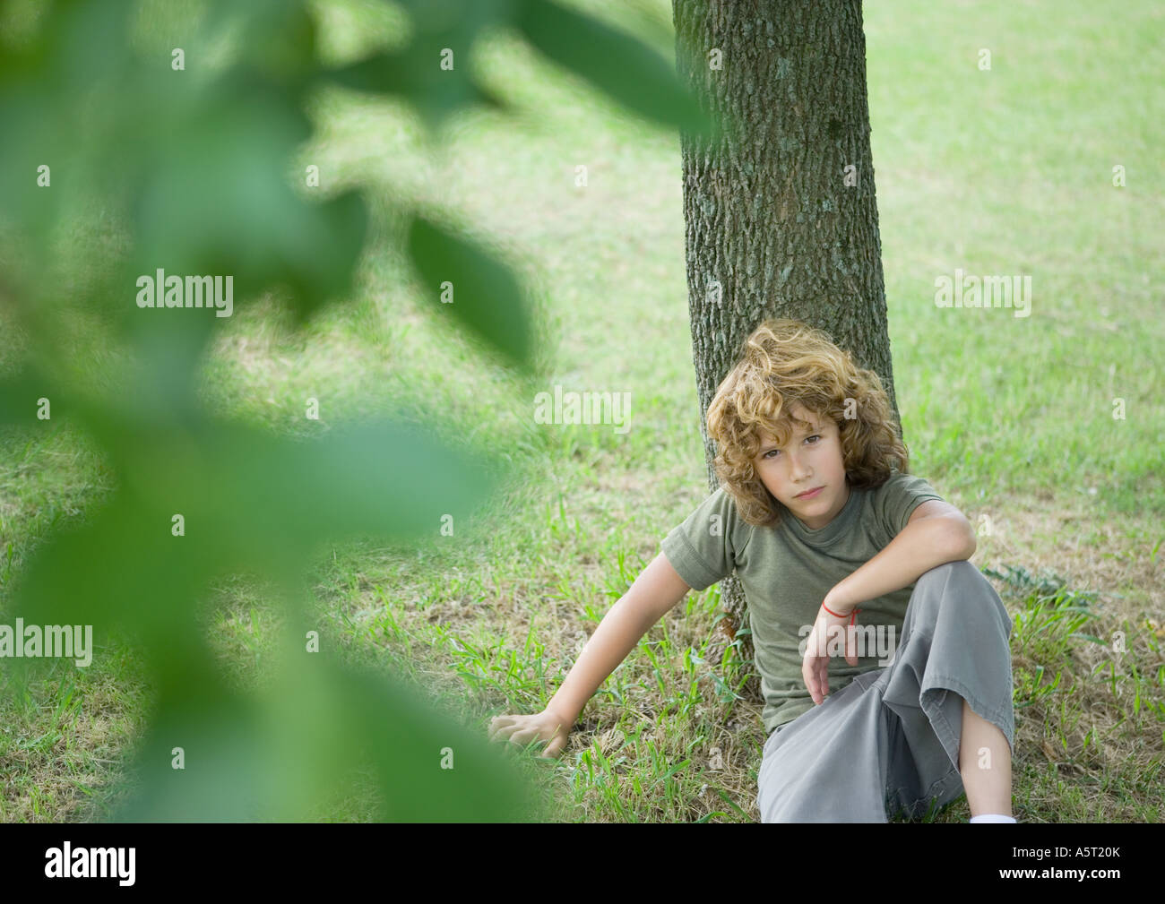Boy sitting on ground, leaning against tree Stock Photo - Alamy