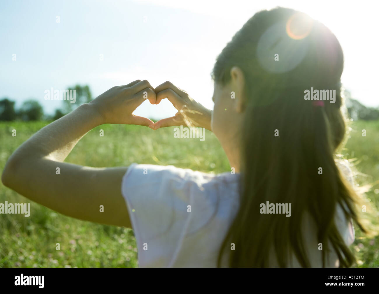 Girl in field, making heart shape with hands, rear view Stock Photo - Alamy