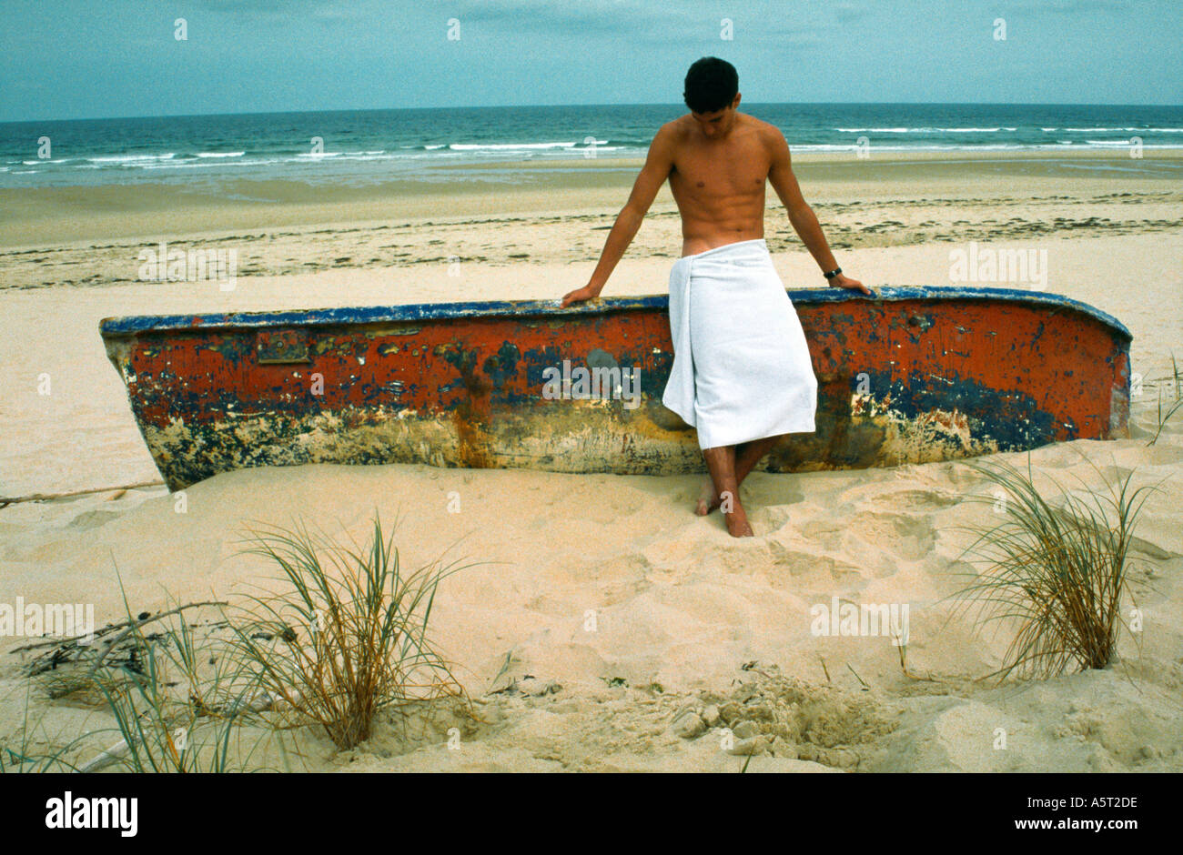 young muscle man lean on a boat end up on the beach Stock Photo - Alamy