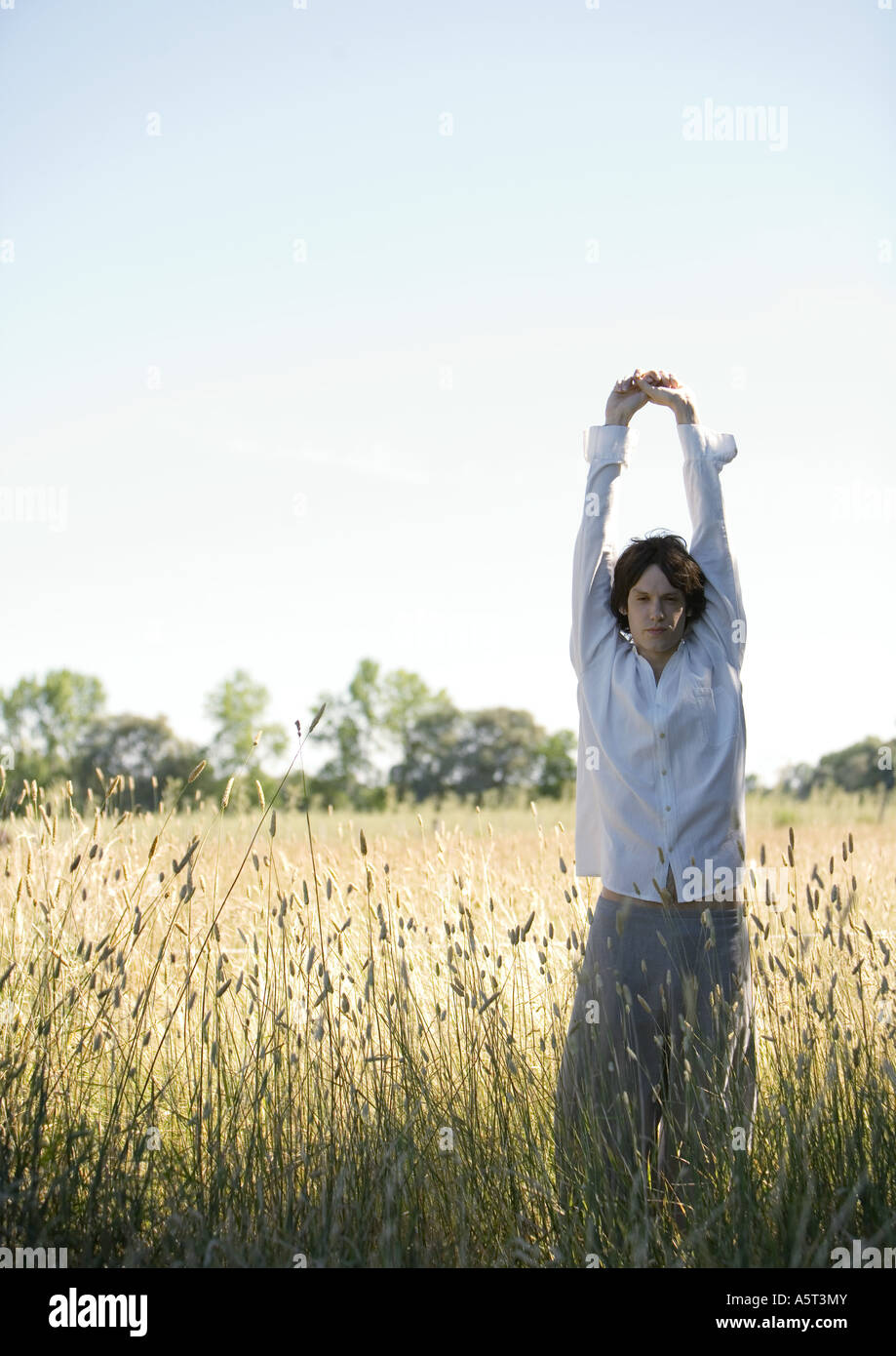 Man standing stretching arms over head in field Stock Photo - Alamy