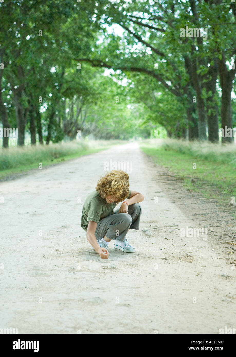 Boy crouching in middle of dirt road Stock Photo - Alamy