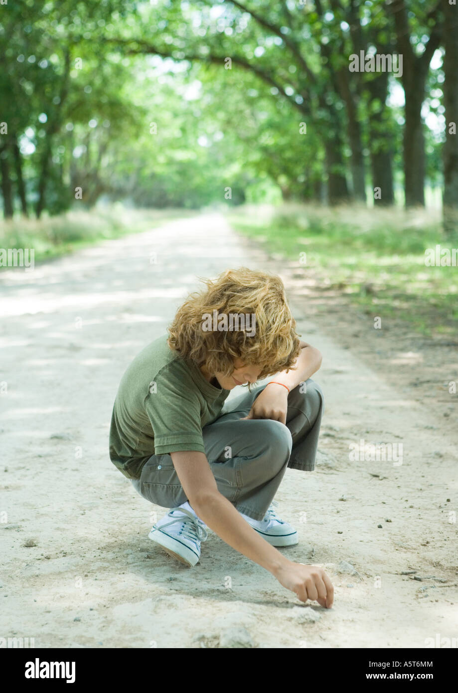 Boy crouching in middle of dirt road Stock Photo - Alamy