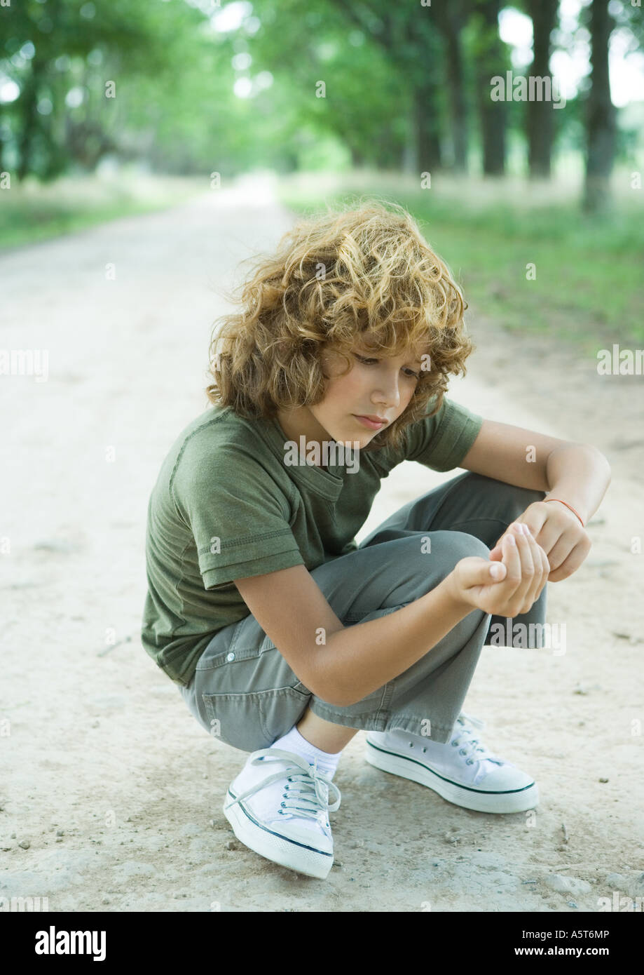 Boy crouching in middle of dirt road, looking at pebbles Stock Photo ...