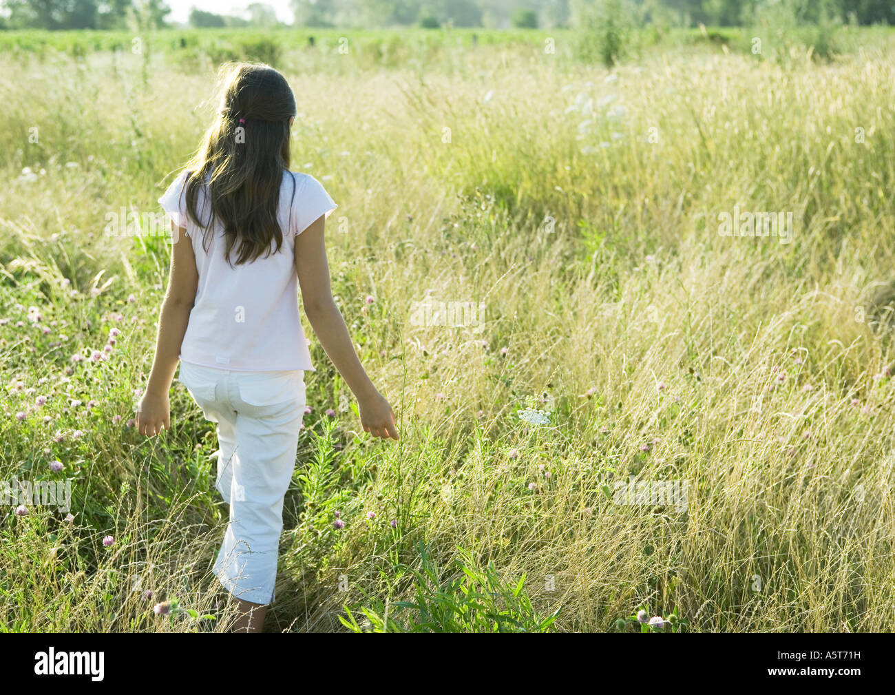 Girl walking through tall grass in field Stock Photo - Alamy