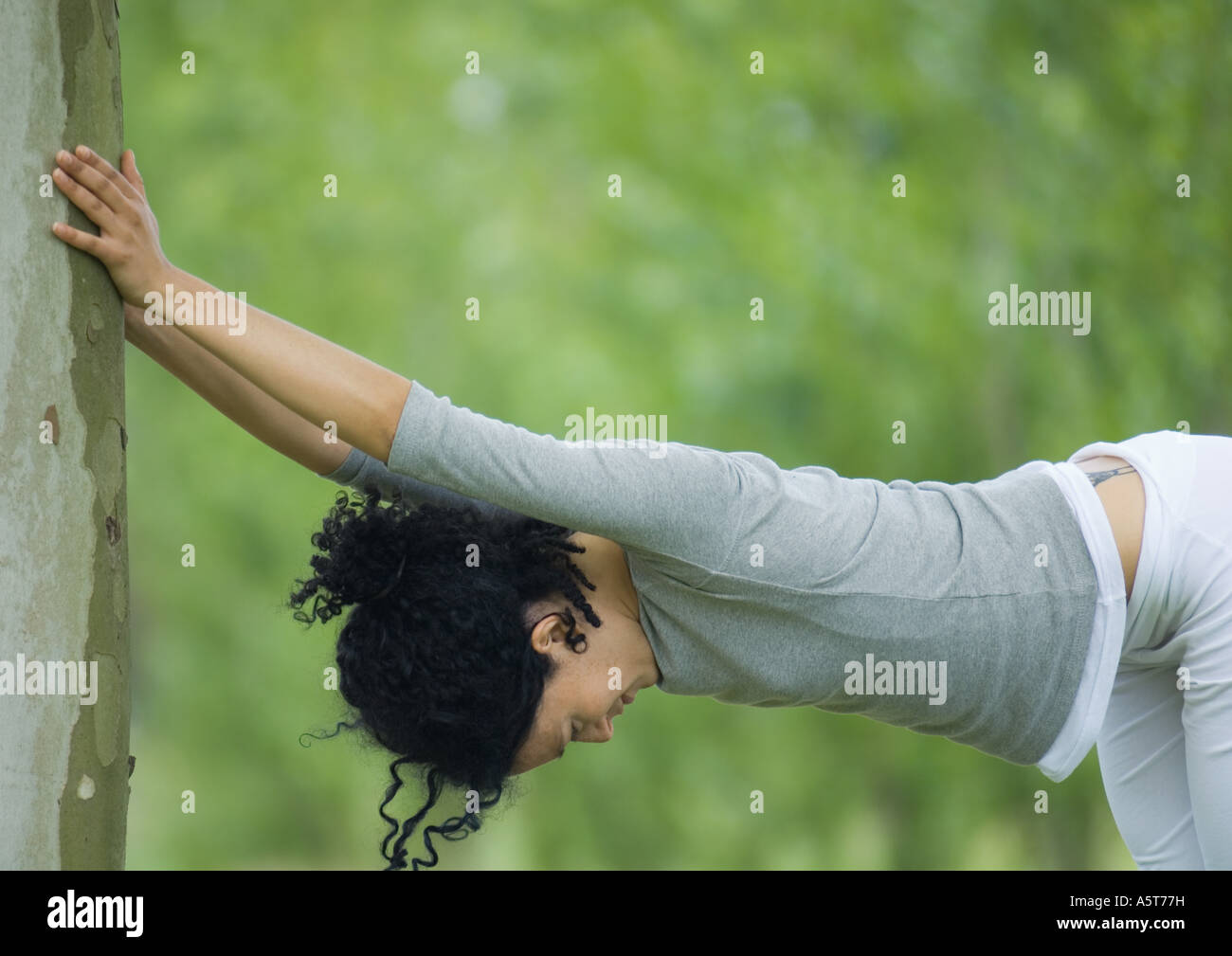 Young woman stretching against tree Stock Photo - Alamy