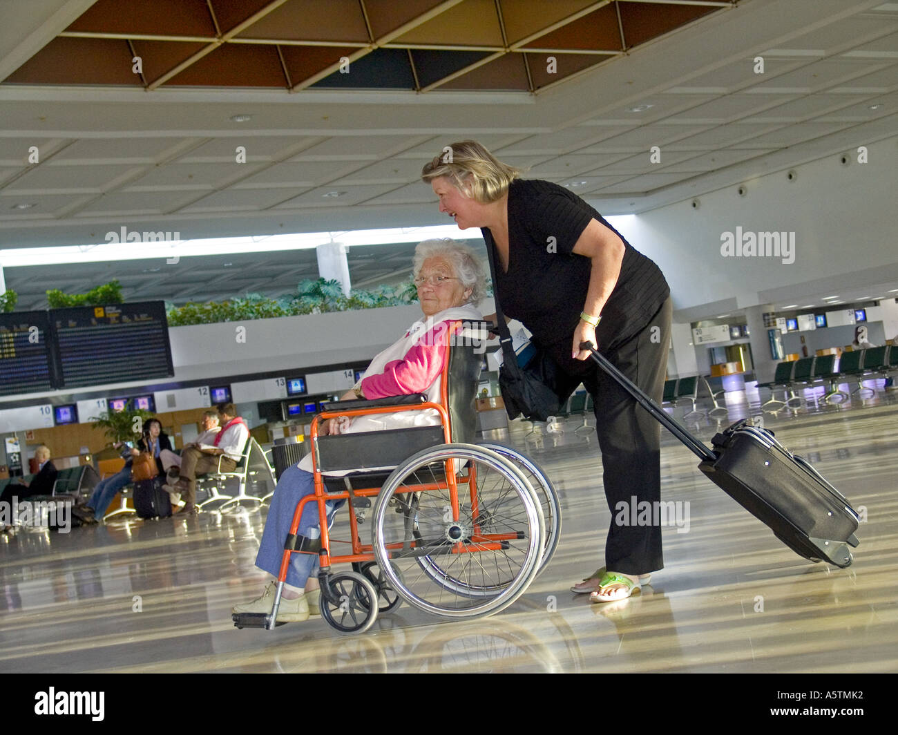 Elderly woman in wheelchair with companion carer on airport concourse ...
