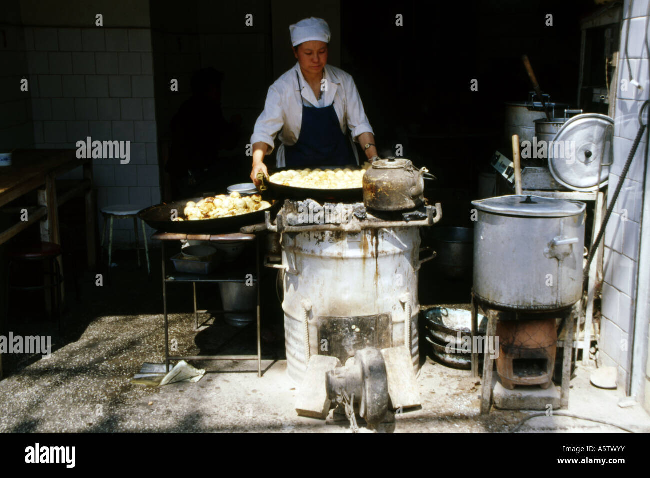 Local man cooking snacks in large wok placed on top of charcoal burning ...