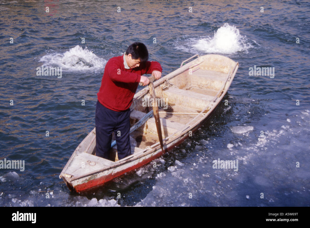 Local man in small boat breaking the ice on lake in the forbidden city ...