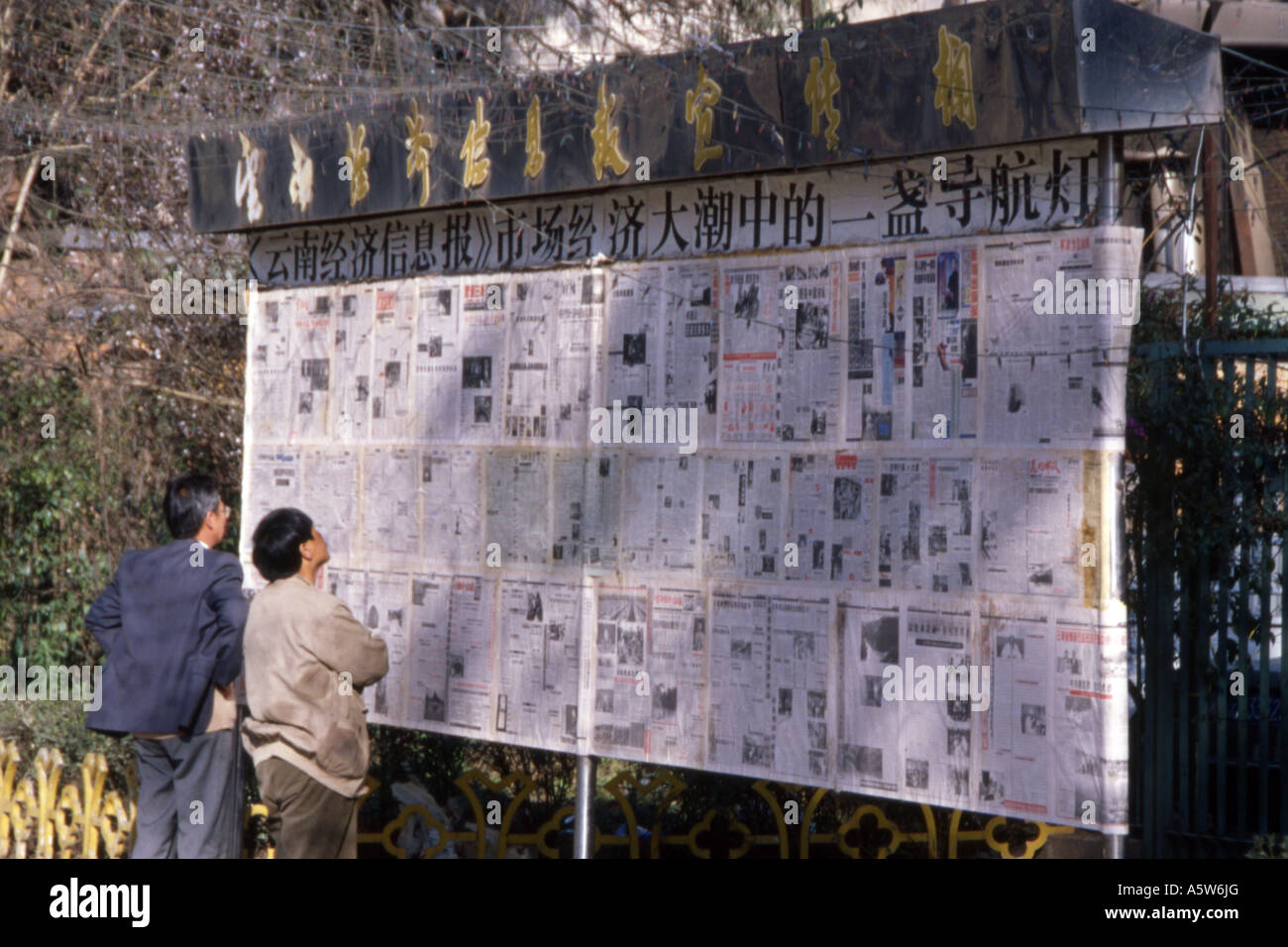 Two local men reading newspapers from traditional street hoarding hi ...