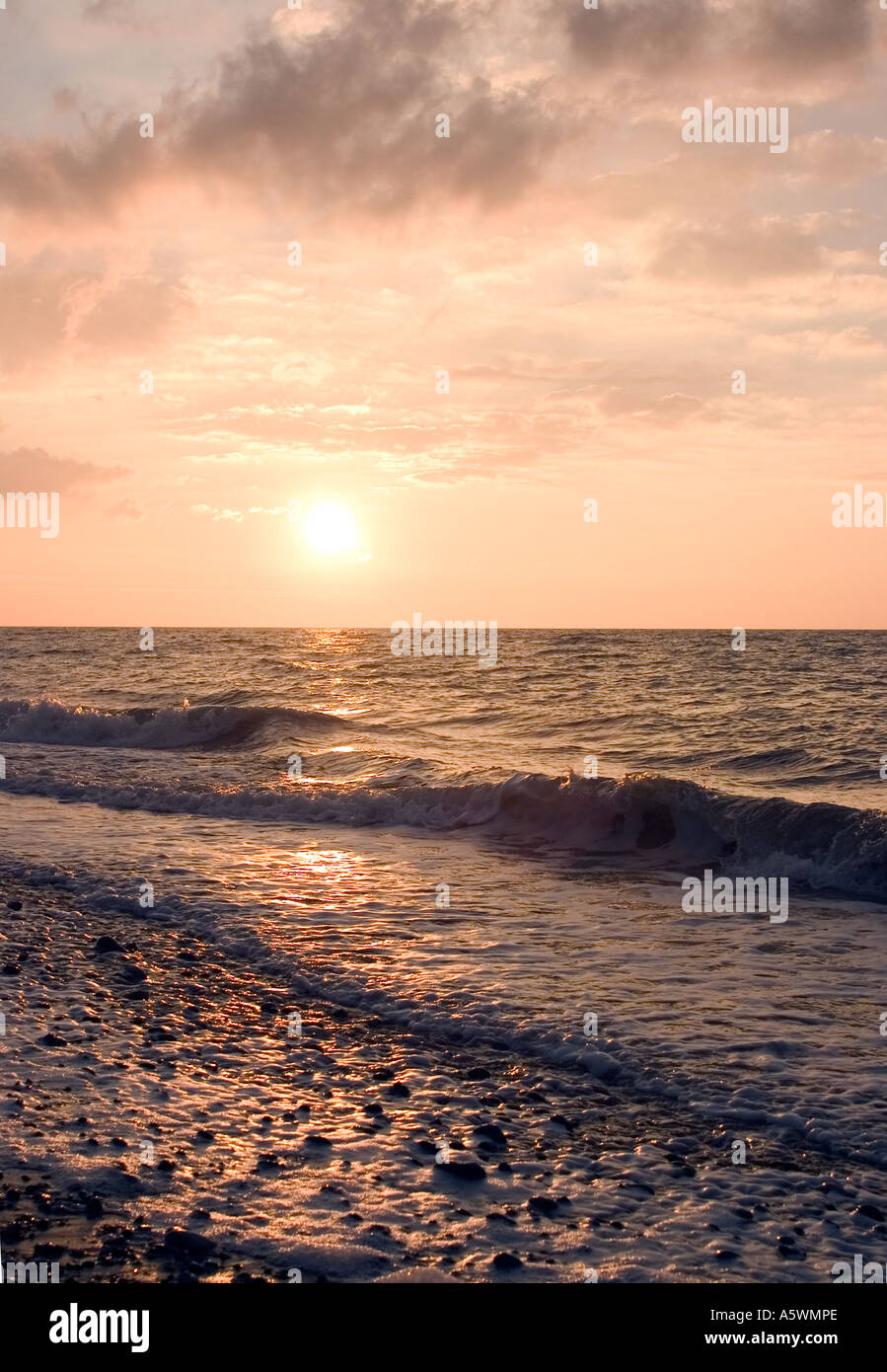 Sun setting into a clam sea with warm sky and clouds Stock Photo - Alamy
