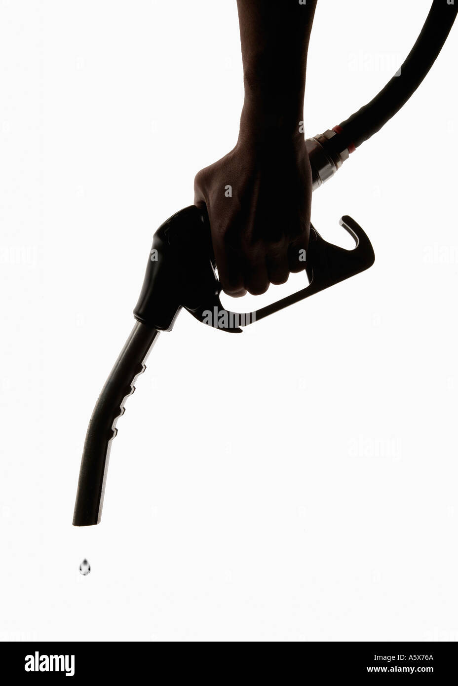 HAND HOLDING PETROL PUMP IN SILHOUETTE WITH SINGLE DROP OF FUEL FALLING ...