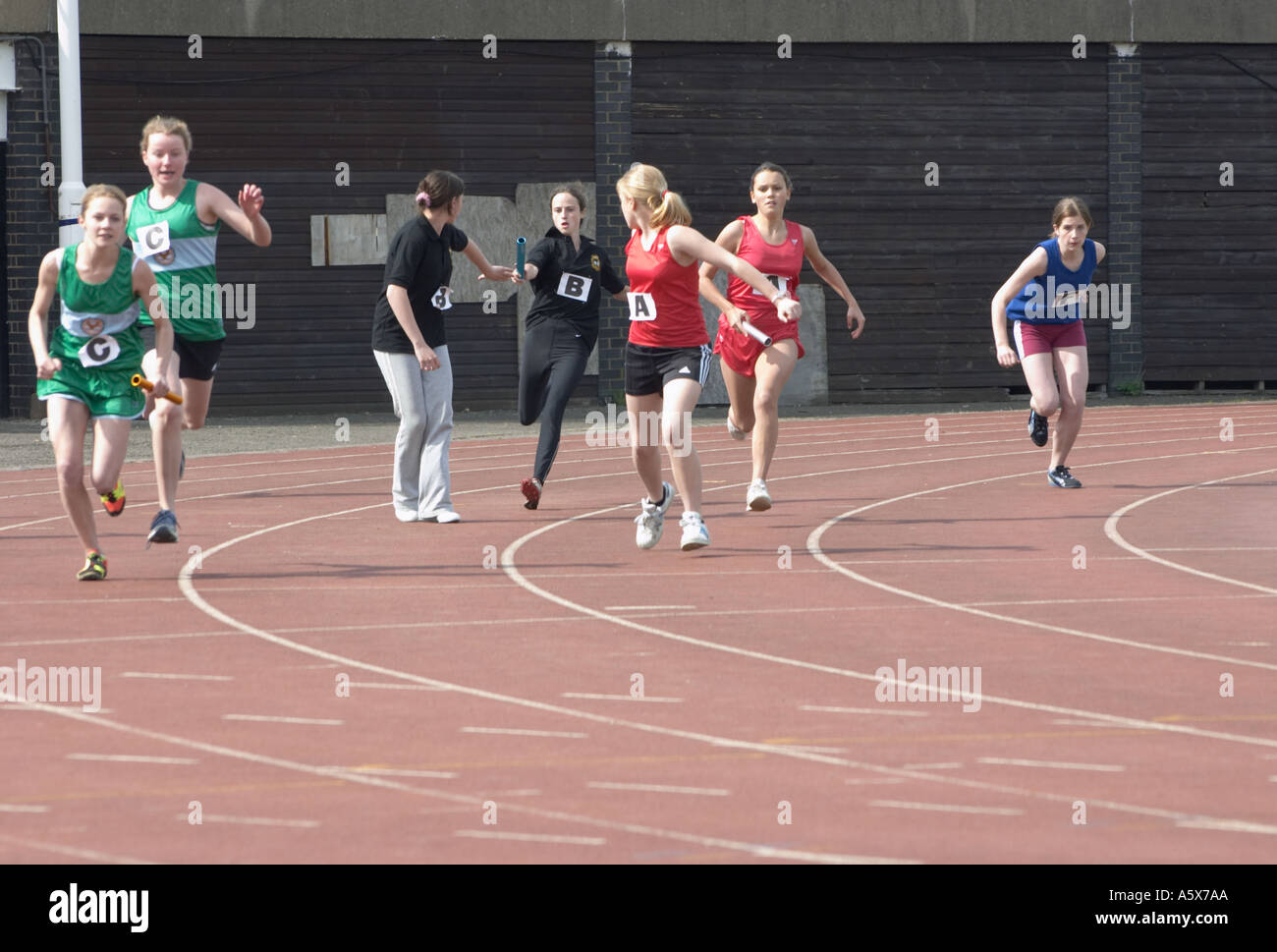 Young women on running track in relay wearing different coloured tops ...