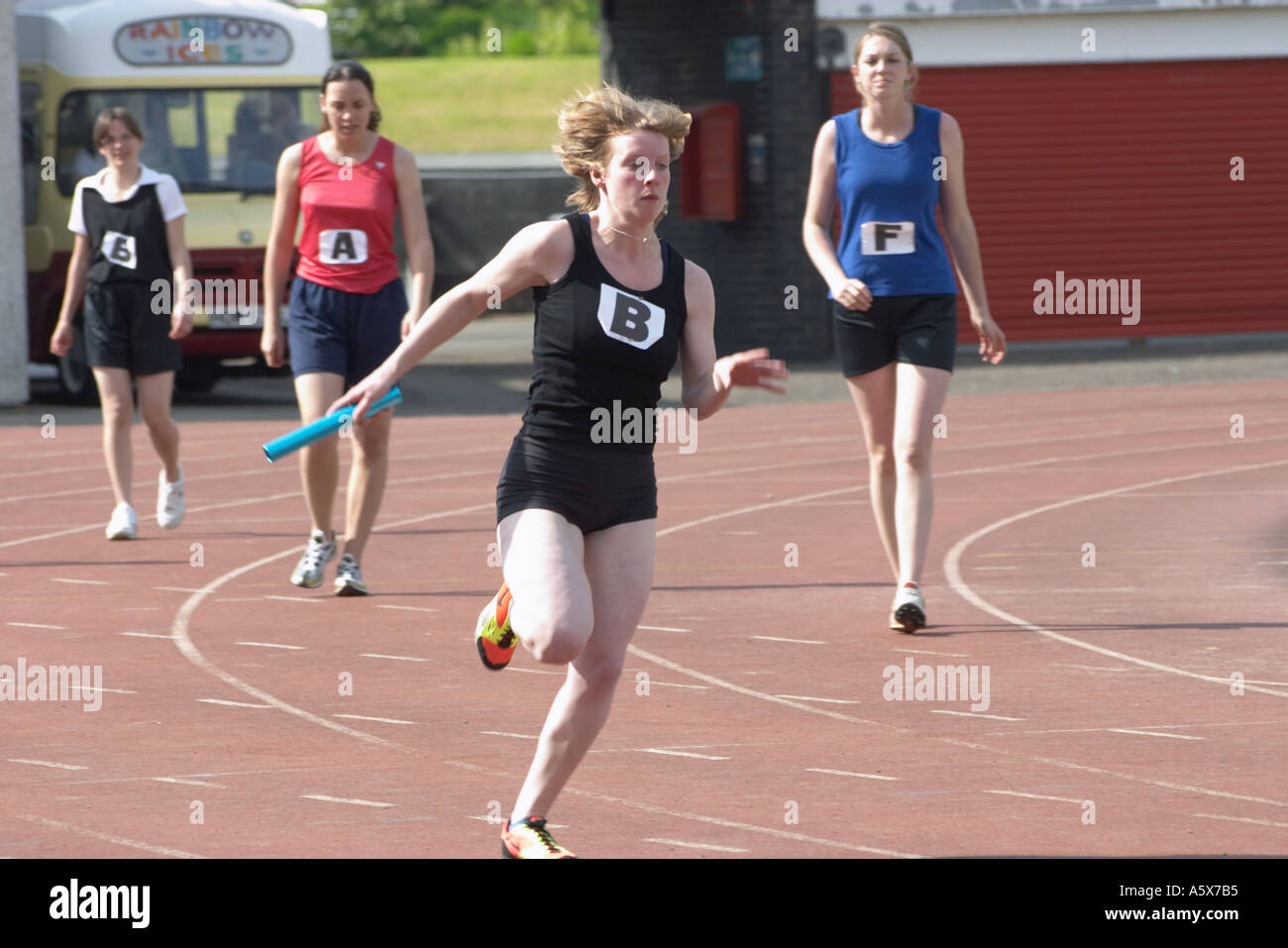 Young women on running track in relay wearing different coloured tops ...