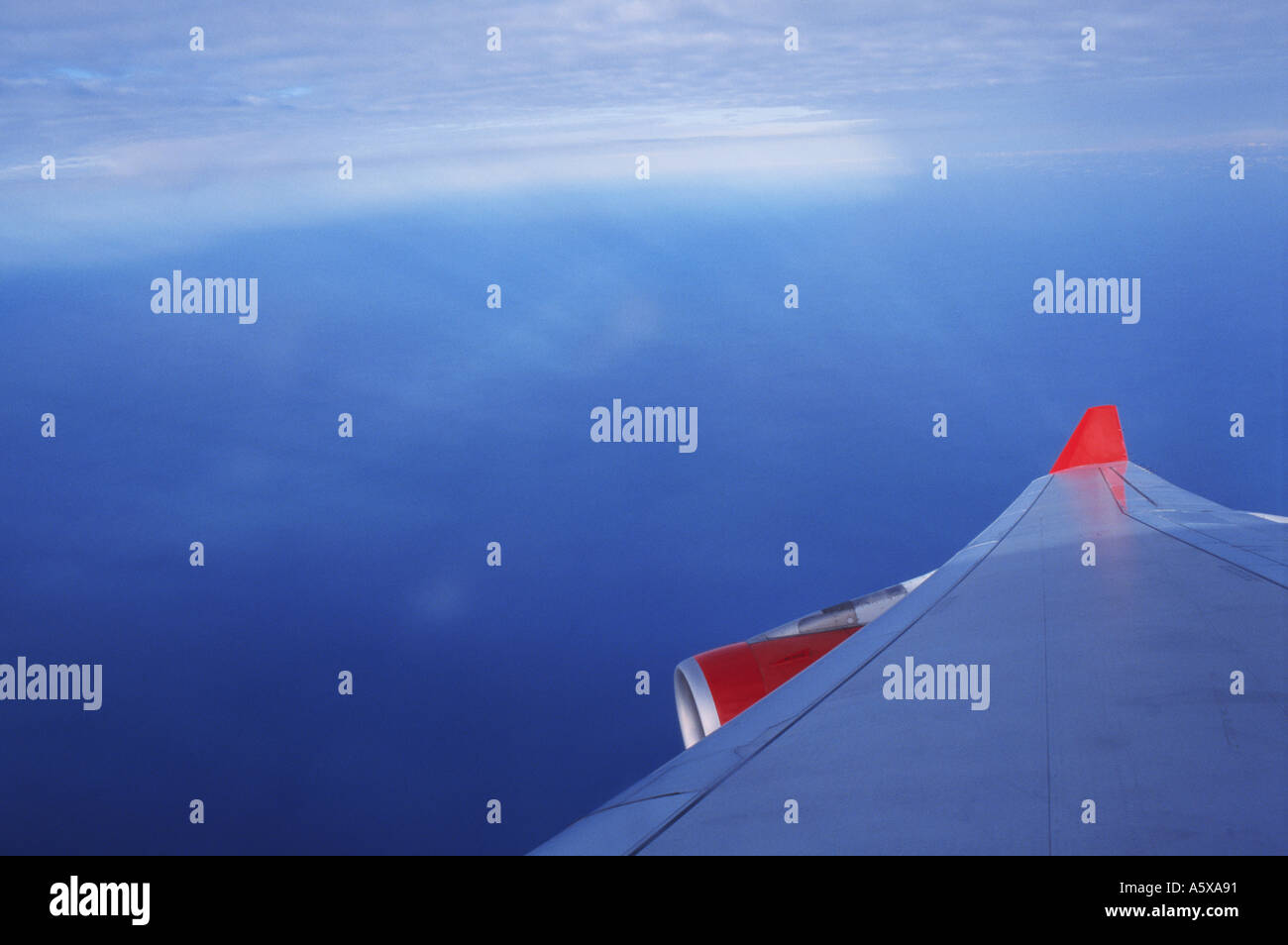 Red engine and wingtip of airplane high above North Atlantic ocean en ...