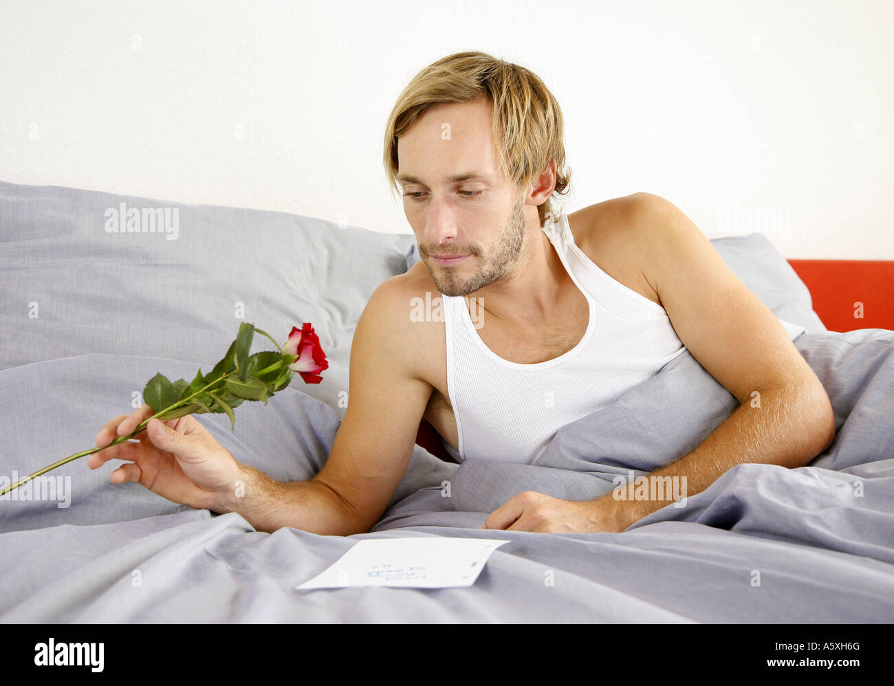 Young man looking at love letter holding rose lying on bed Stock Photo ...