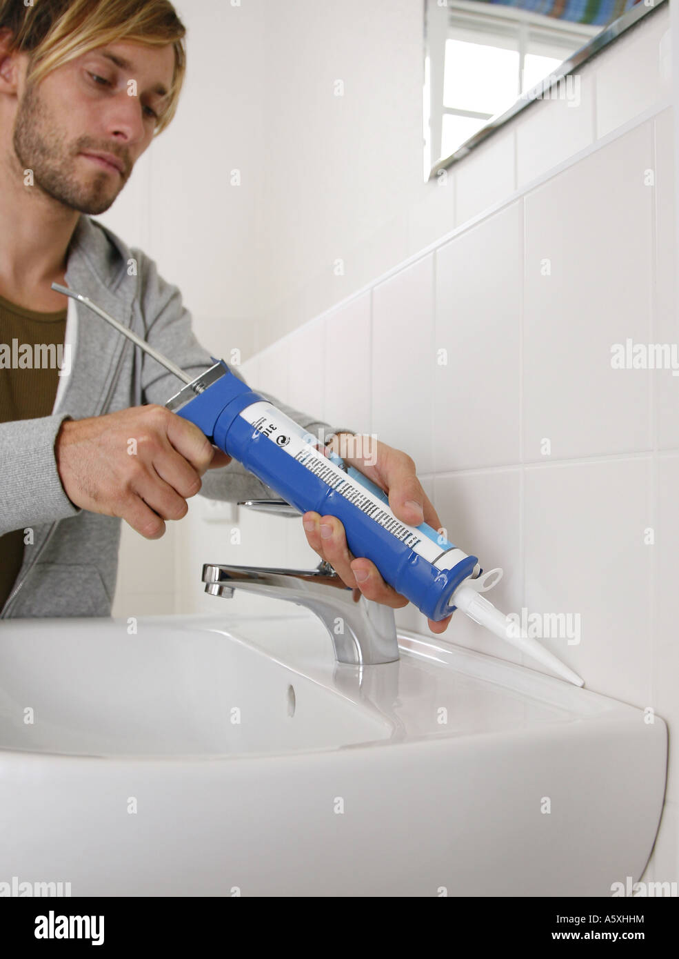 Young man using a silicon applicator gun on a bathroom sink Stock Photo ...