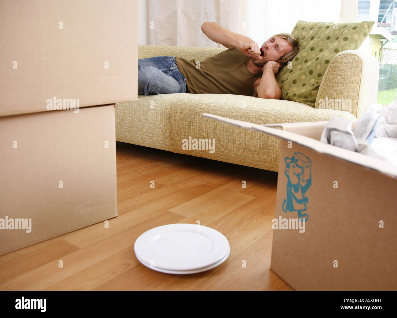 Man lying on sofa yawning stack of boxes Stock Photo - Alamy