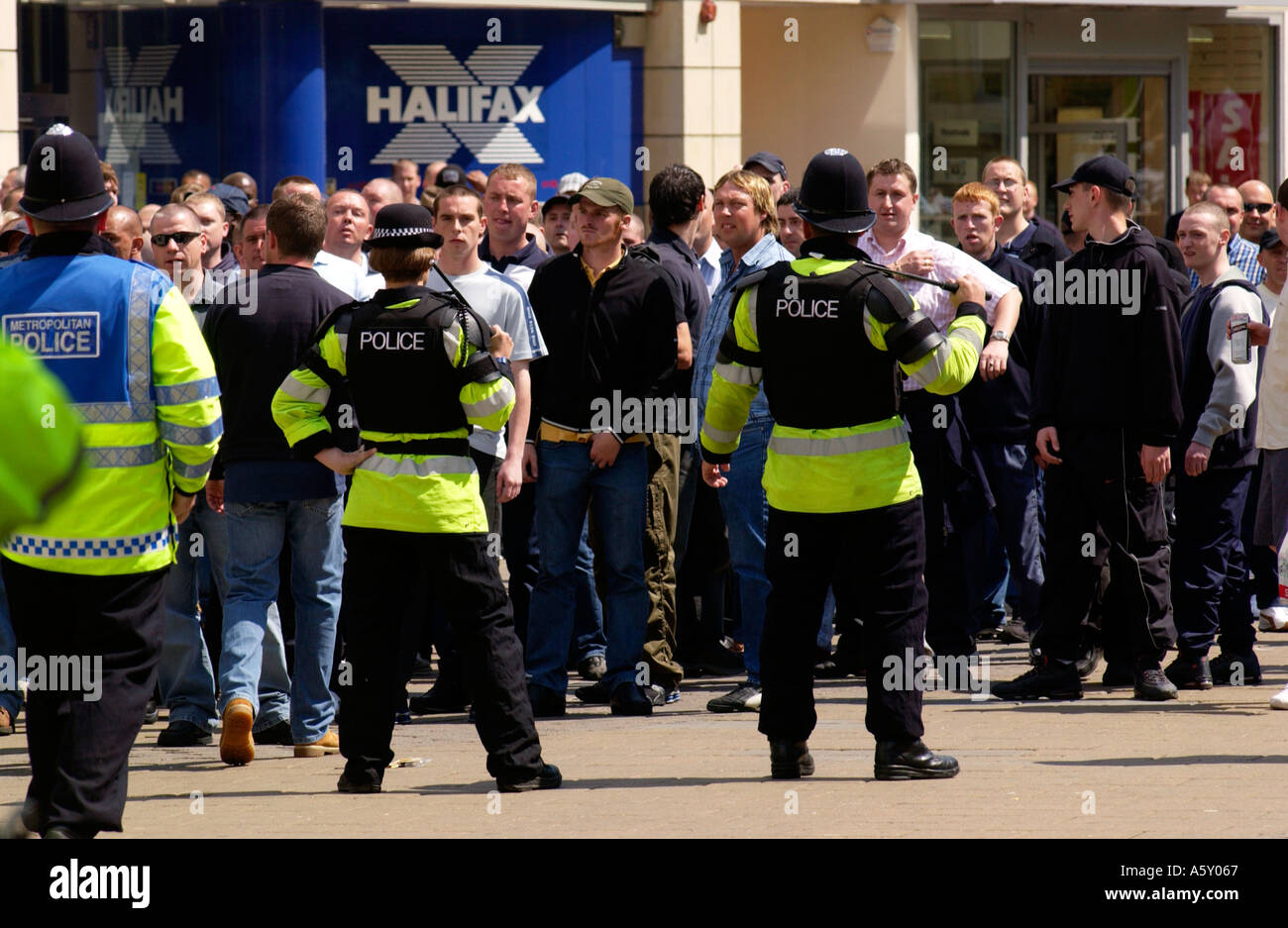 Police officers batons drawn watch over a group of football fans in ...