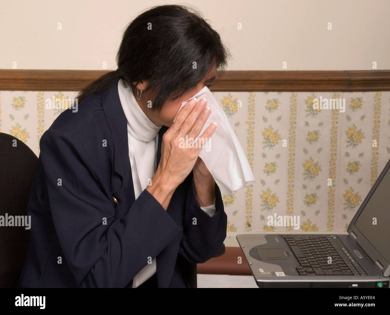 Caucasian female office worker sneezing at her desk, illustrating ...