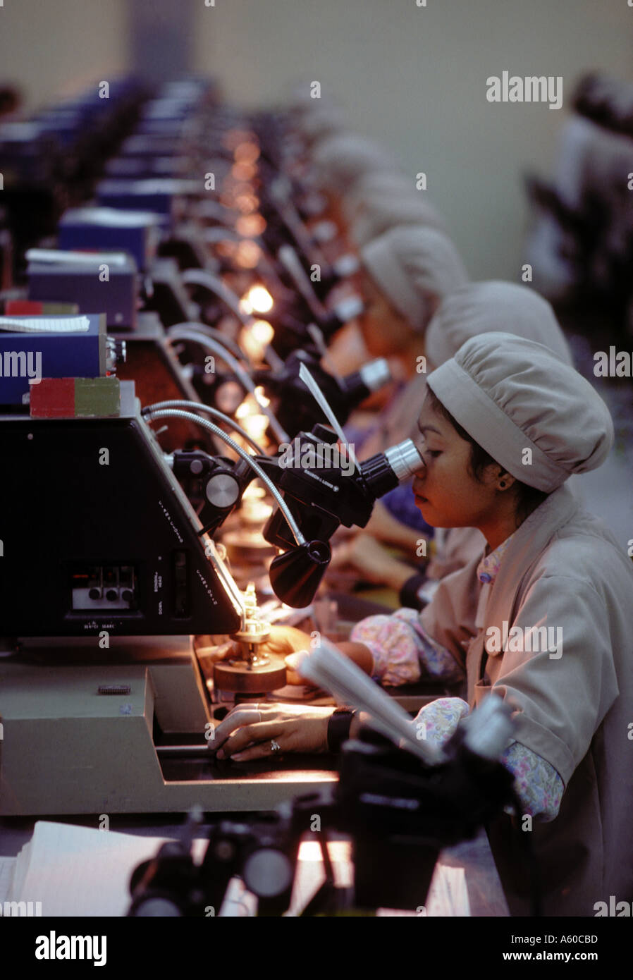 female worker looking through microscope at computer chip assembly ...