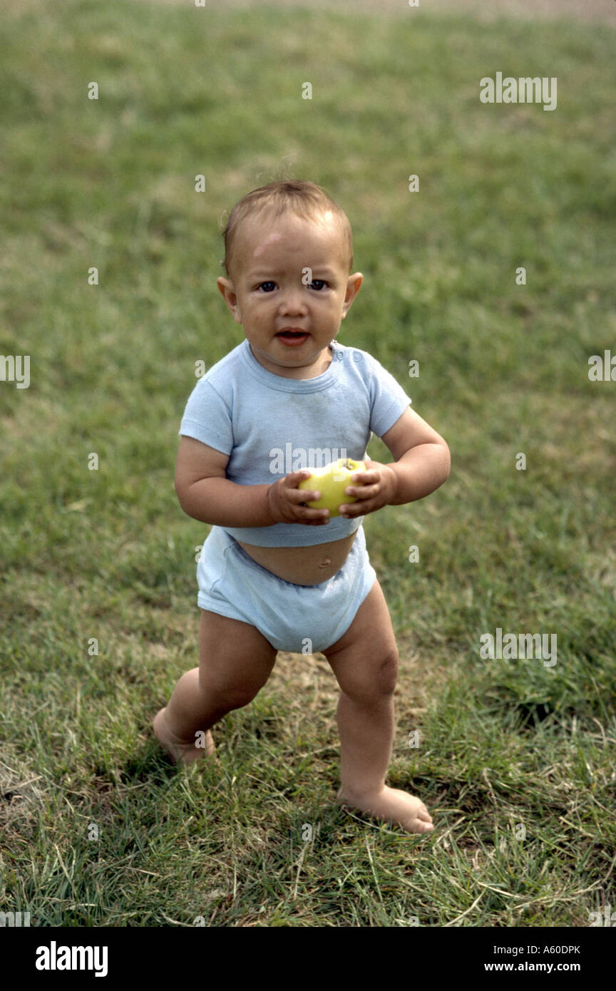 One year old boy walking around on the grass while eating an apple ...