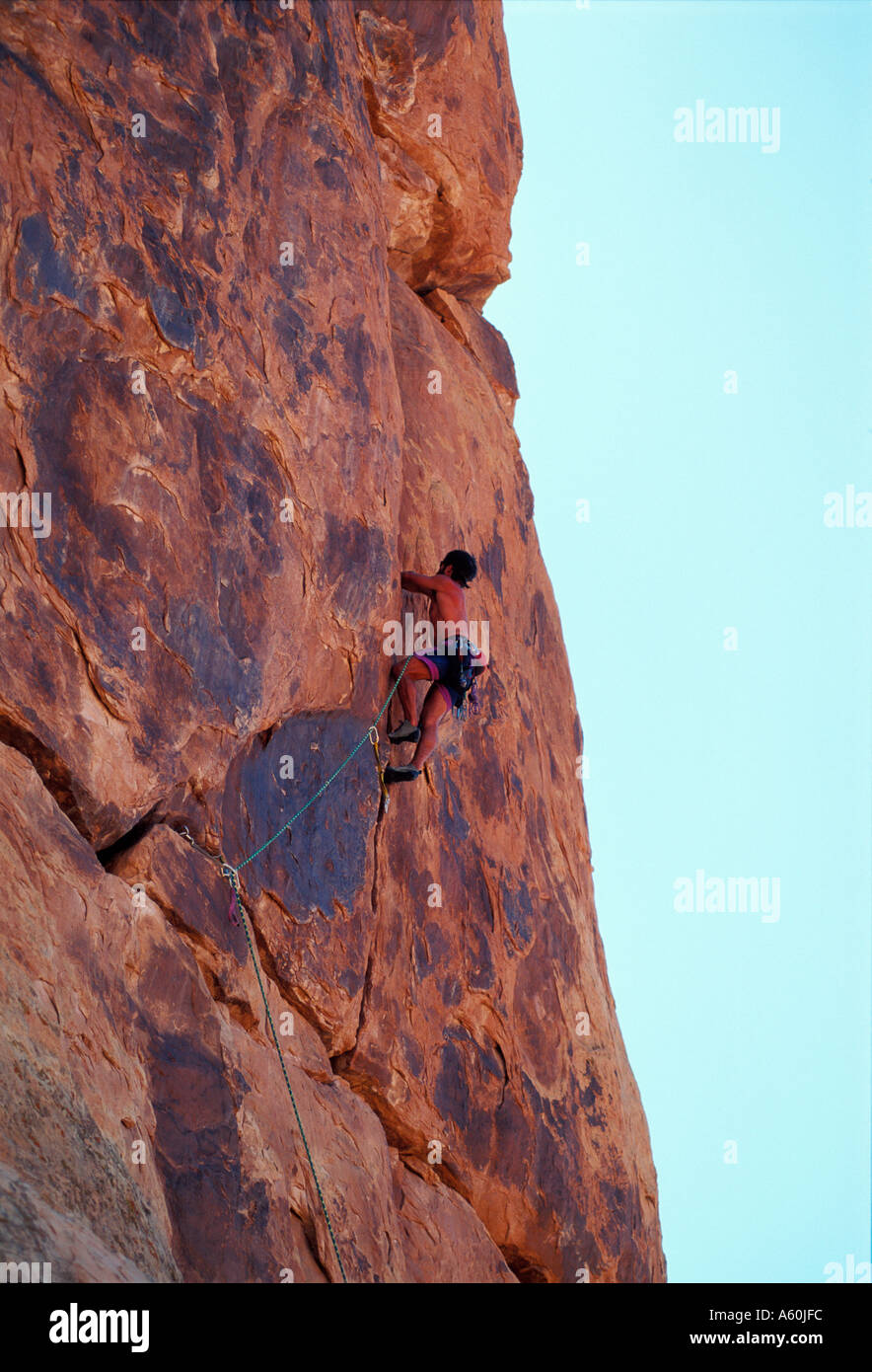 A male rock climber works his way up a crack in a vertical rock face ...