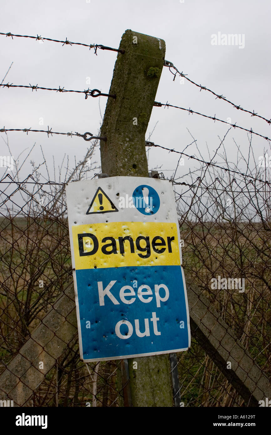 Blue and yellow metal danger keep out sign peppered with bullet holes ...
