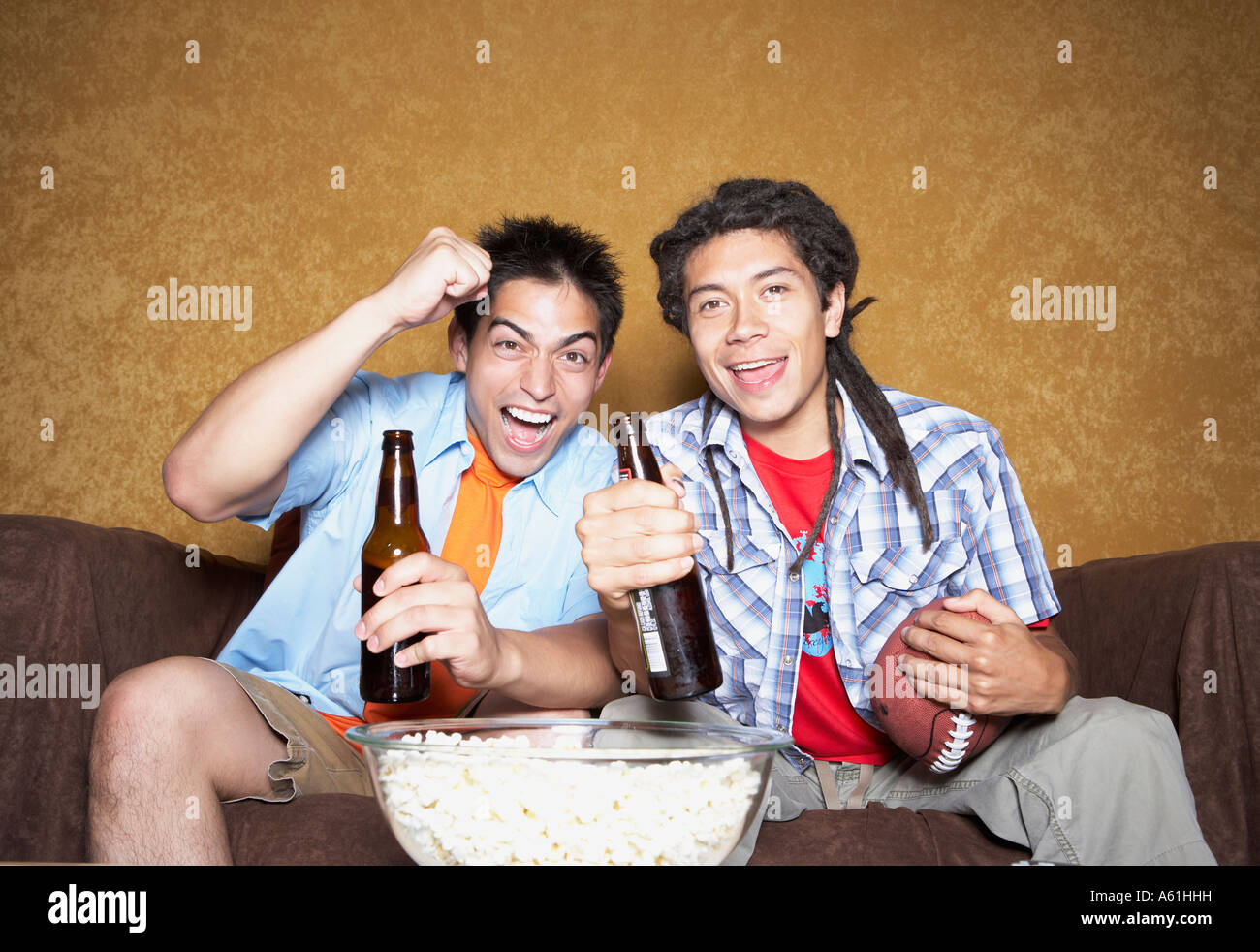 Two young men cheering on sofa with football Stock Photo - Alamy
