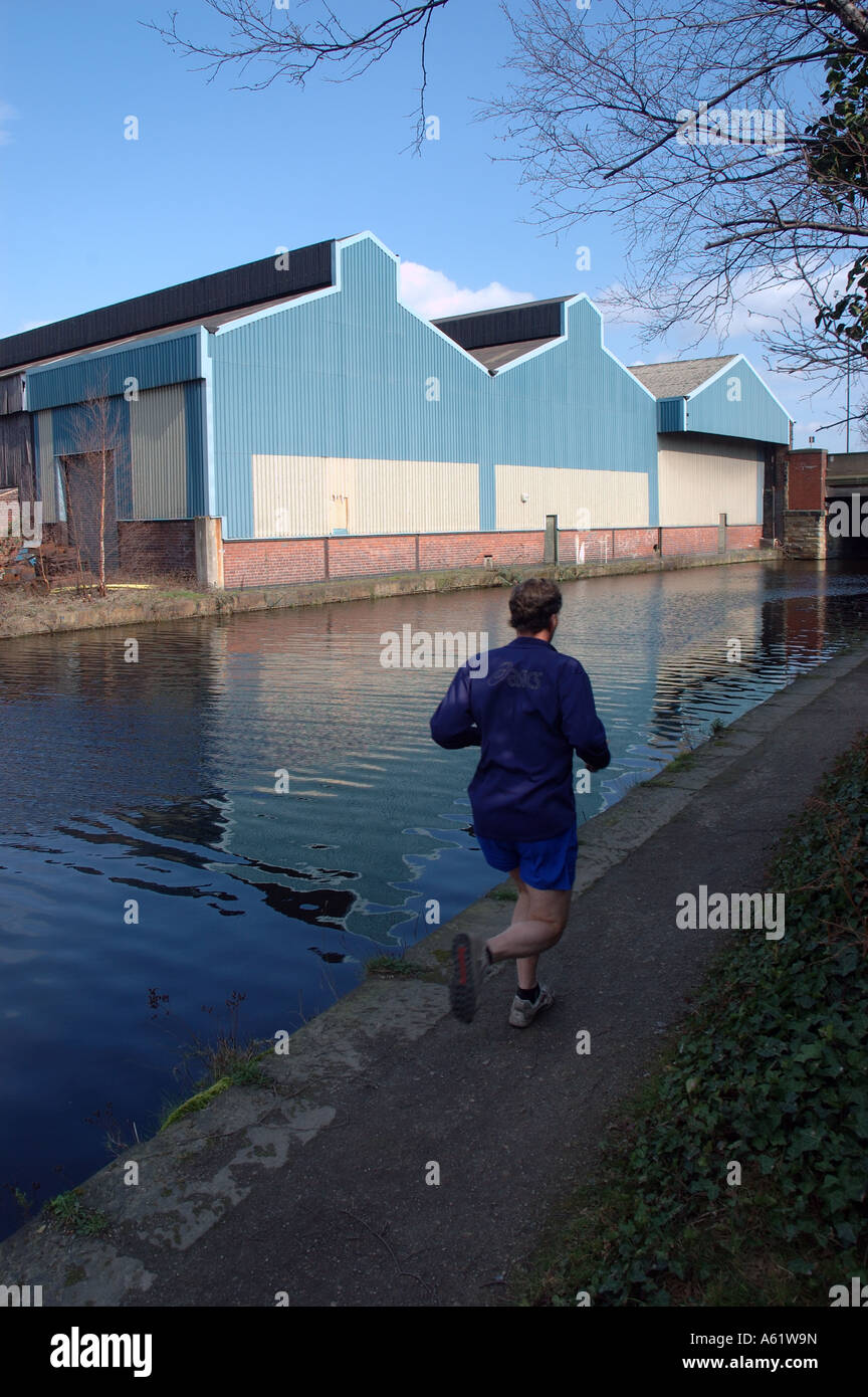 Jogger on canal bank with industrial buildings in the background Stock ...