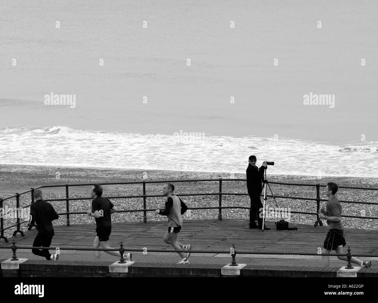 Four male athletes running past a photographer using a camera on a ...
