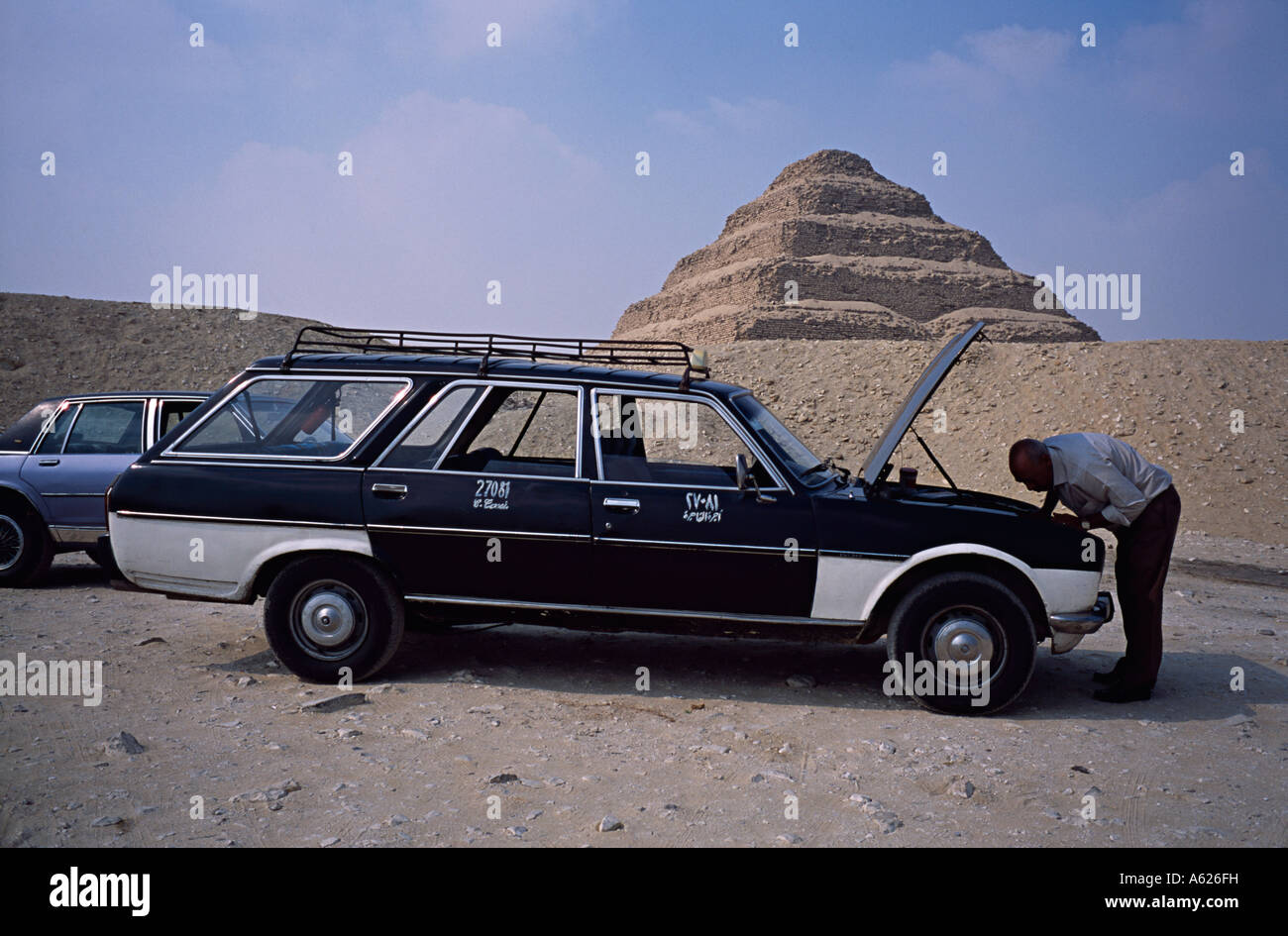 Taxi driver examining his engine in front of the Step Pyramid, Cairo ...