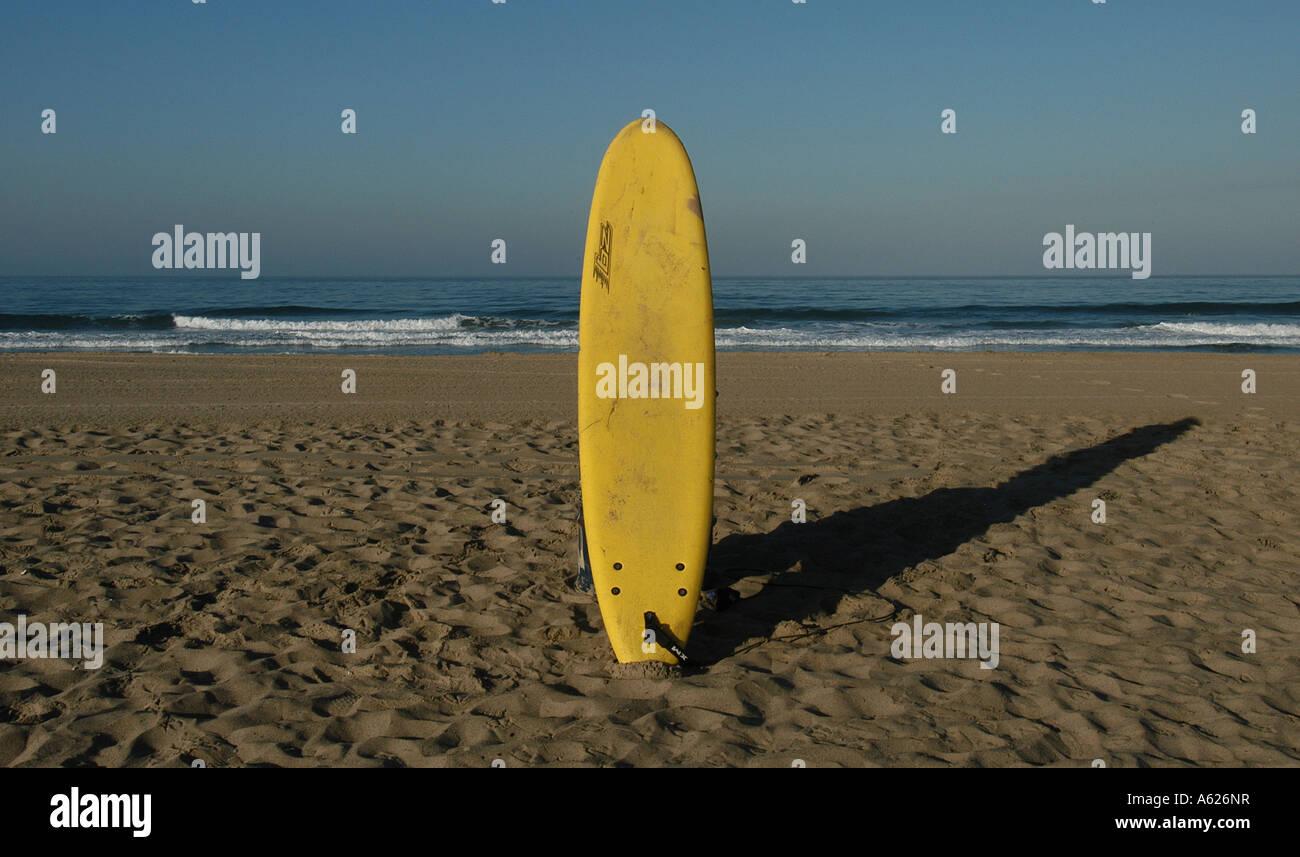 A lone yellow surf board stands on a sandy beach as the waves break off ...