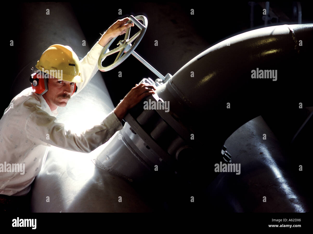 A graphic portrait of a man turning a valve at a petro chemical storage ...