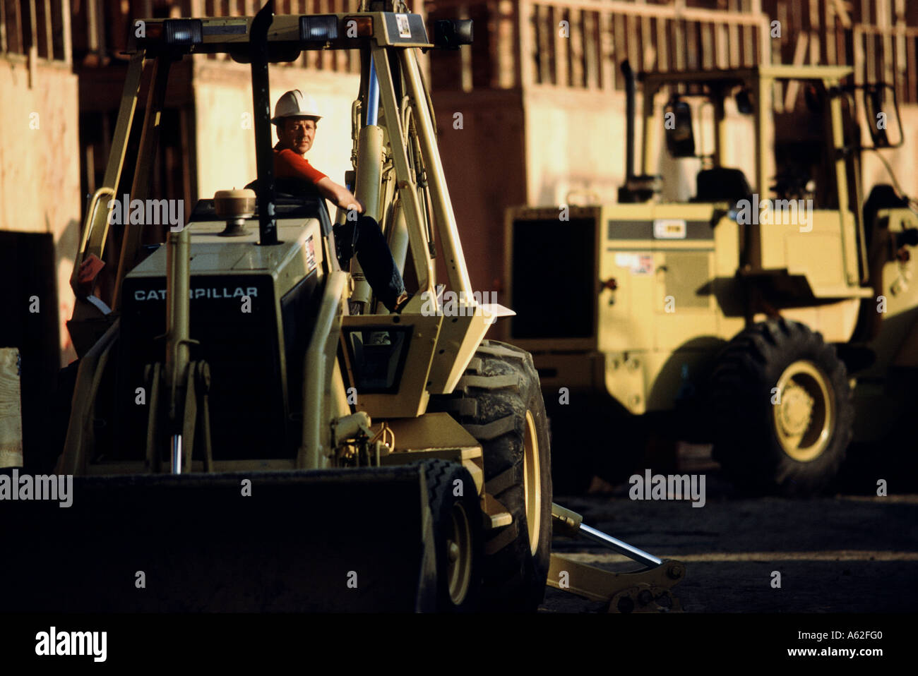 A construction worker operating a backhoe at a building site turns to ...