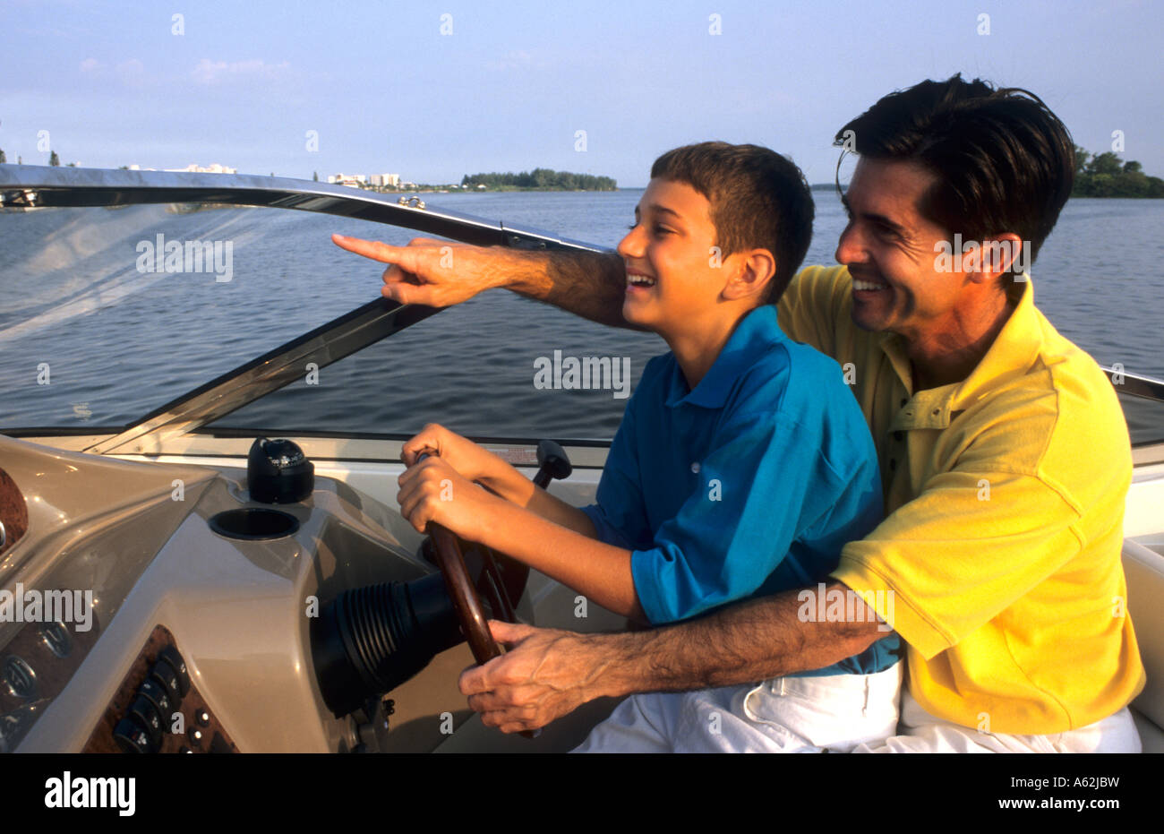 Hispanic father and son sharing the fun of boating and driving the boat ...